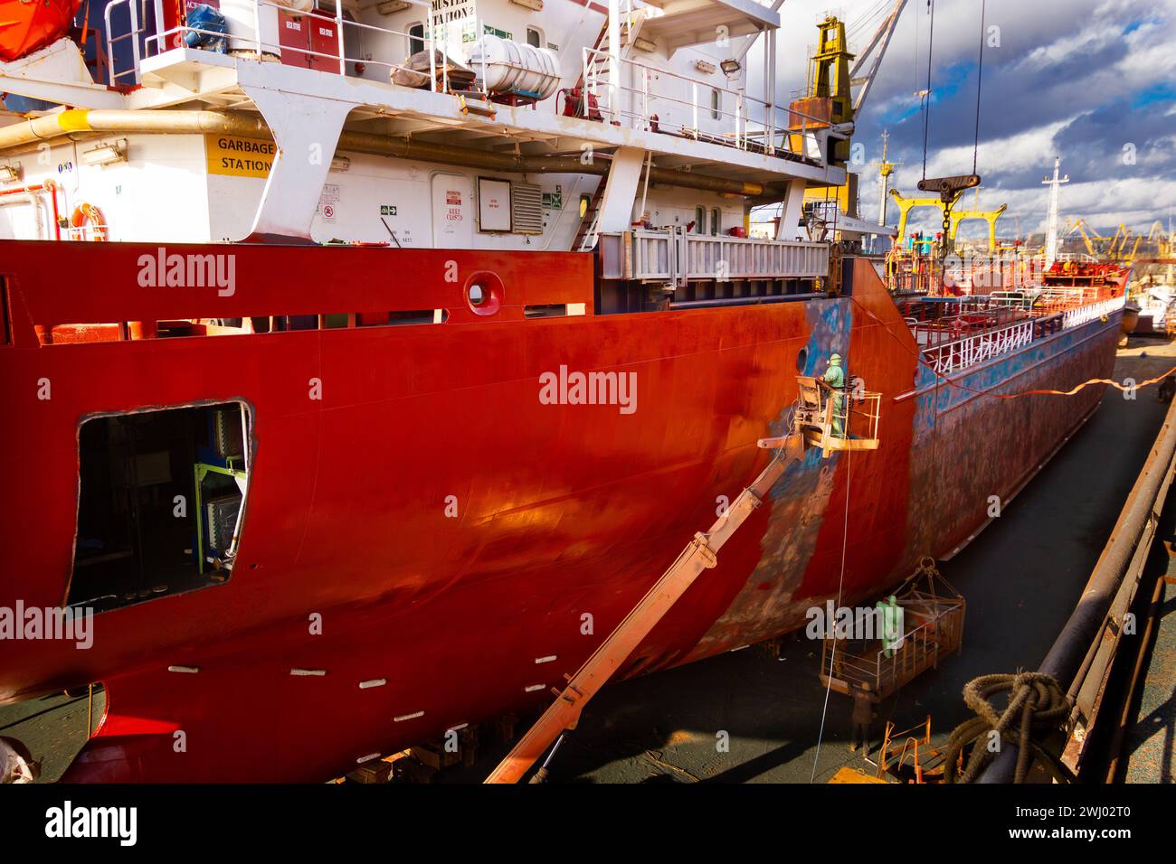 Ship undergoing maintenance in floating dock. Workers paint, repair ...