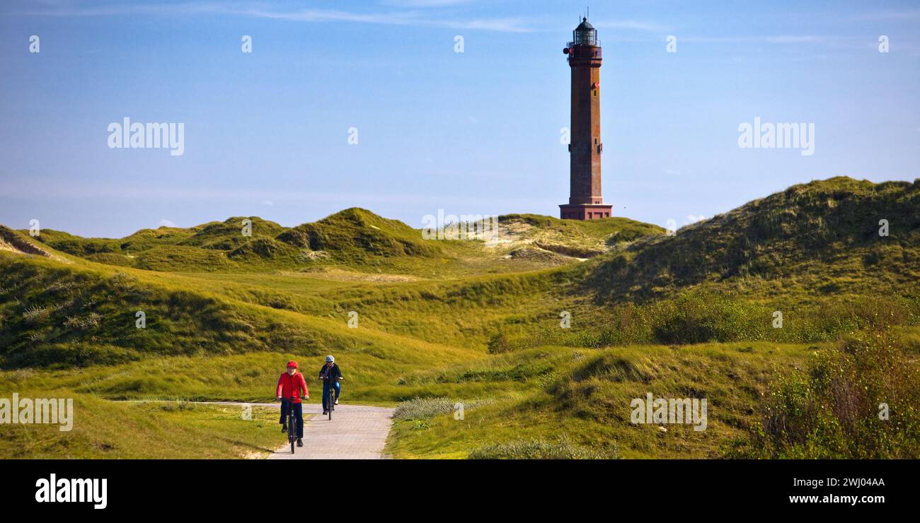 Large Norderney lighthouse in the dune landscape with cyclists ...