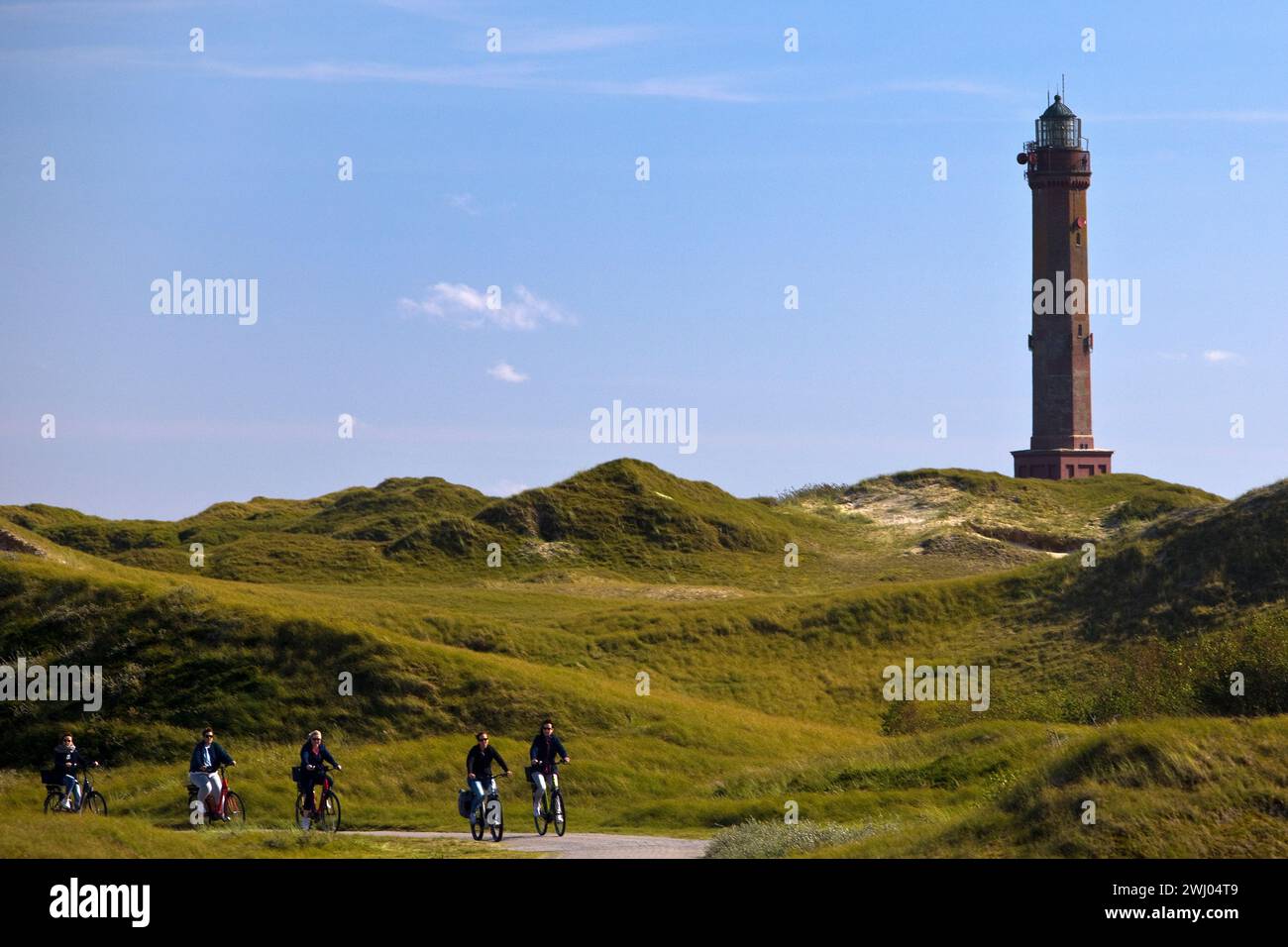 Large Norderney lighthouse in the dune landscape with cyclists ...