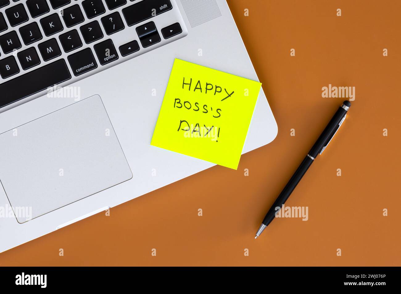Sticky note with phrase Happy Boss Day attached to laptop on brown ...