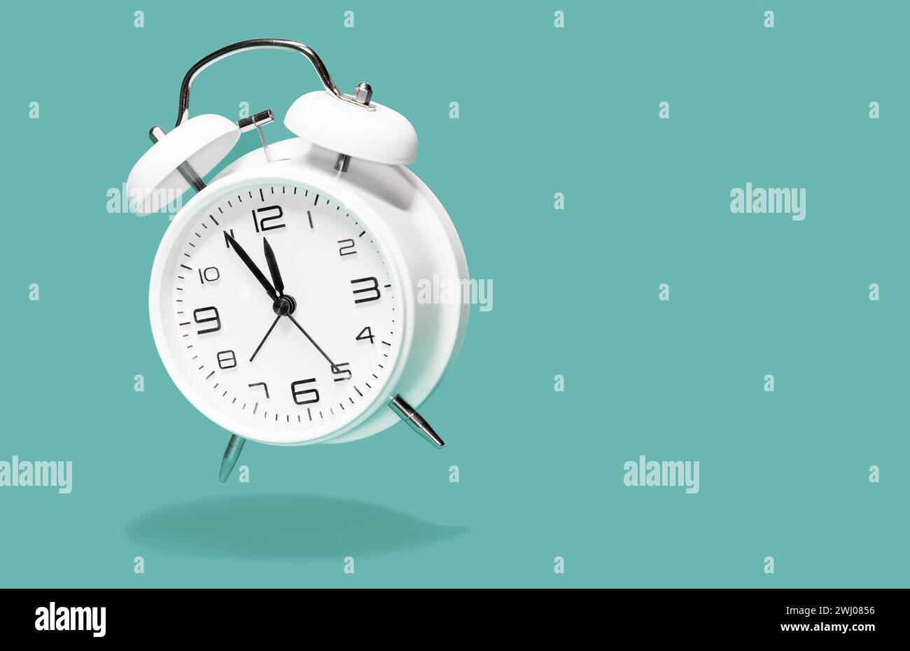 White bell alarm clock hovering over green background. 5 to 12 clock ...