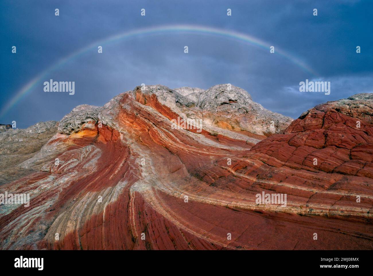 The reddish cliffs under a cloudy sky with a rainbow. White Pocket ...
