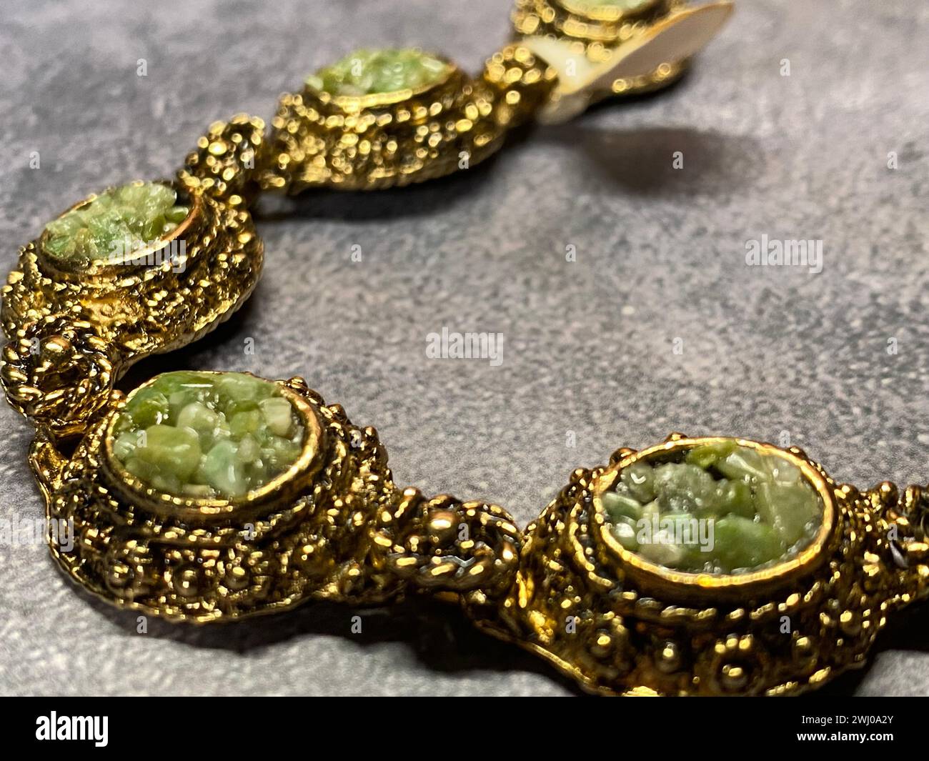 A gold chain adorned with vibrant green gemstones and two distinct ...