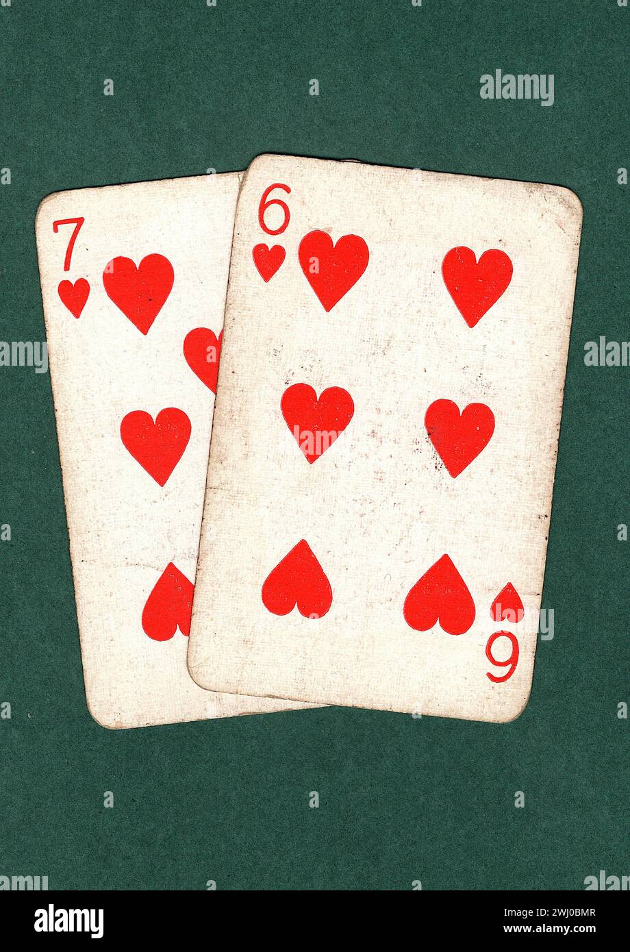 A pair of vintage playing cards showing a six and seven of hearts on a dark green background ...