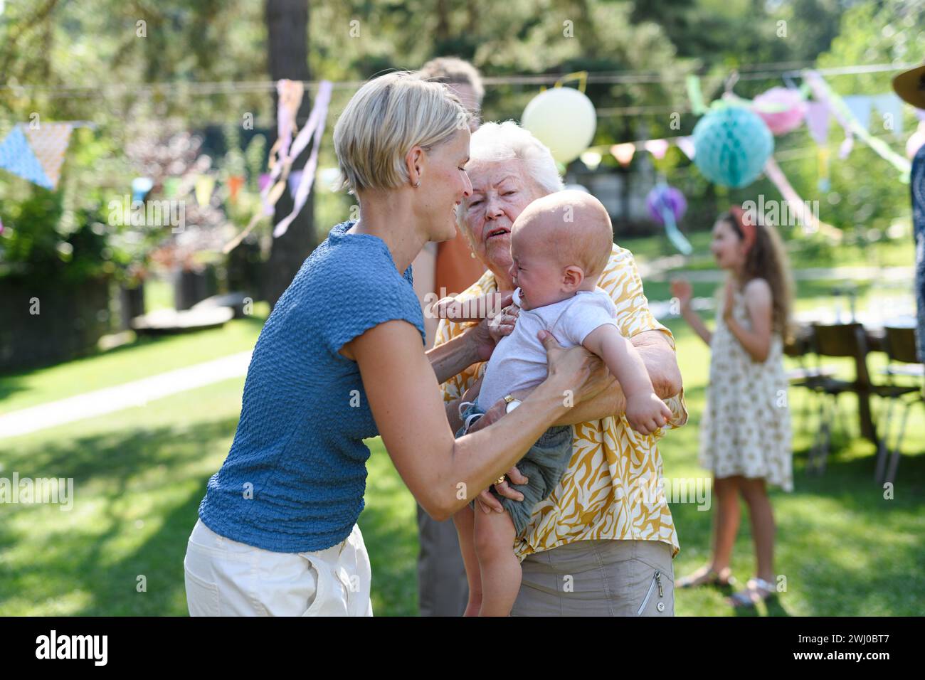 Great-grandmother holding crying little baby in her arms. Family summer ...