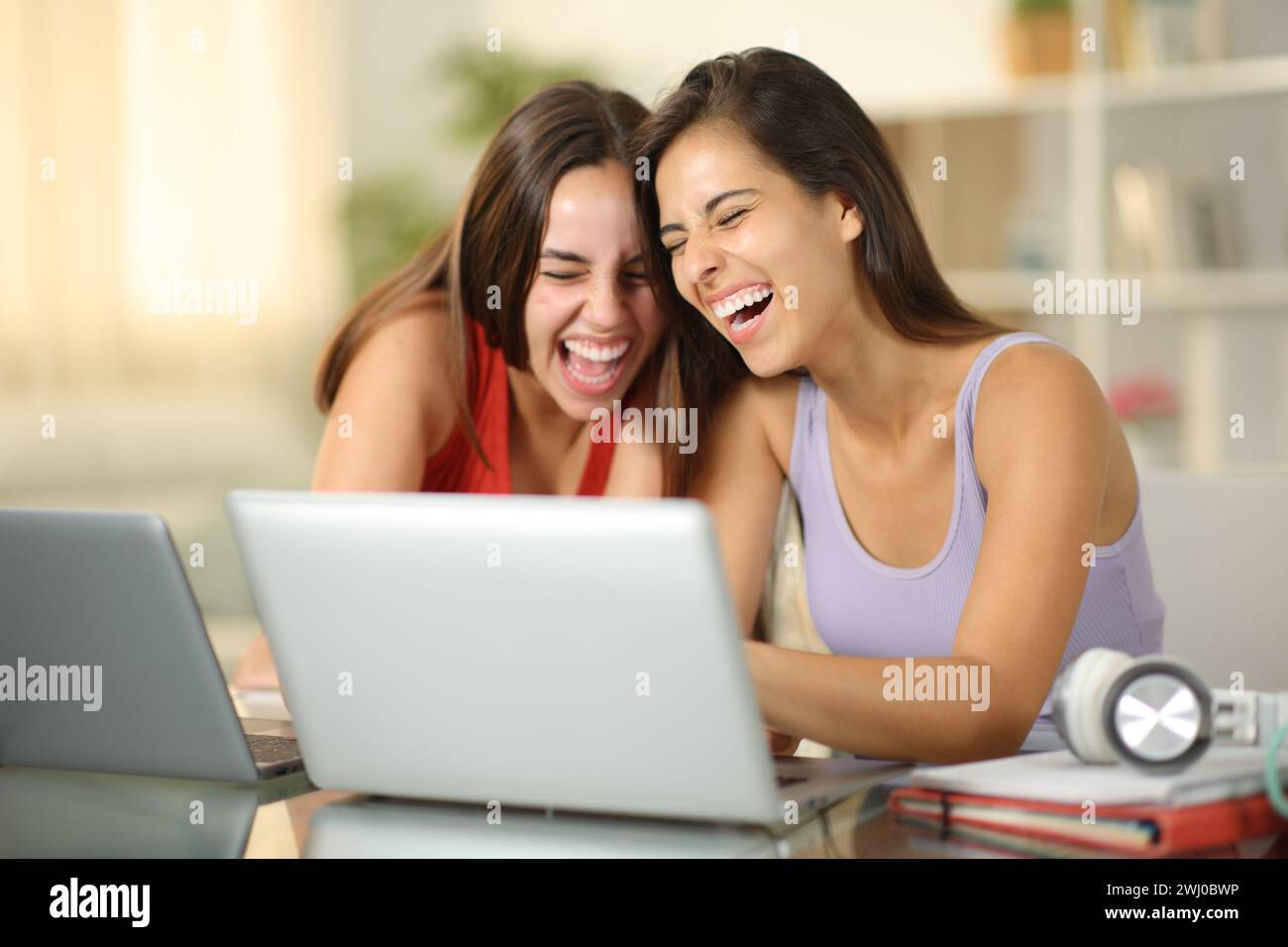 Happy students laughing hilariously watching media on laptop at home ...