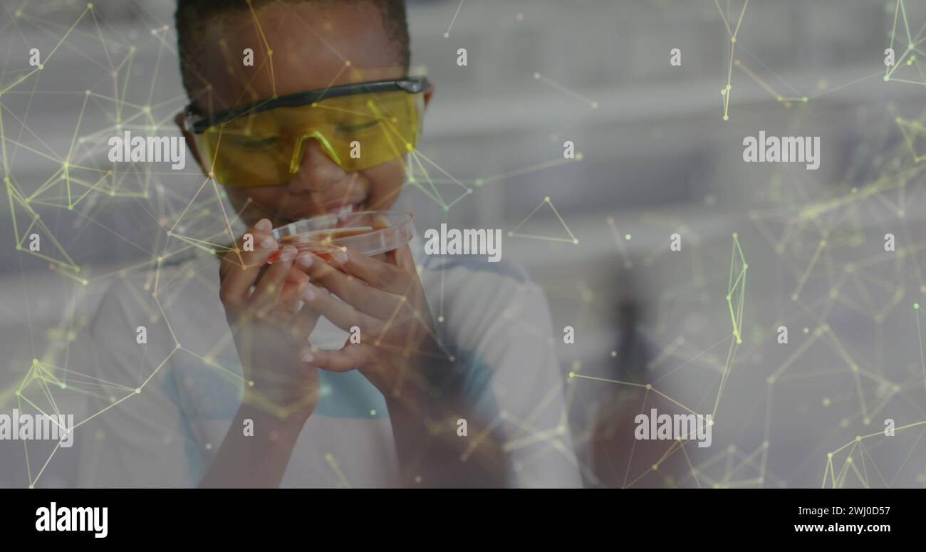 Image of networks over happy african american schoolboy studying petri dish in science class ...