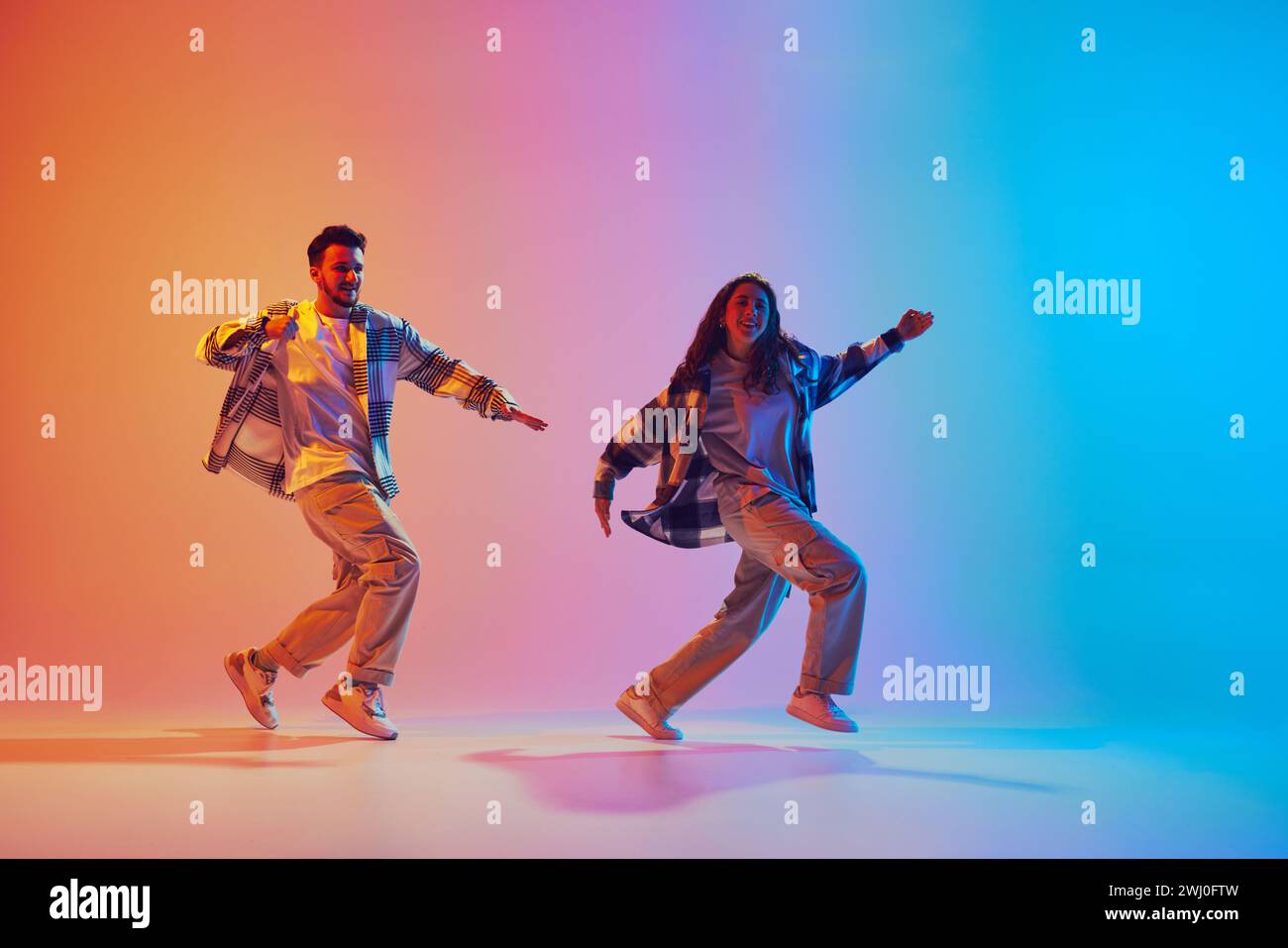 Two joyful dancers in motion, man and woman in neon colorful lighting ...