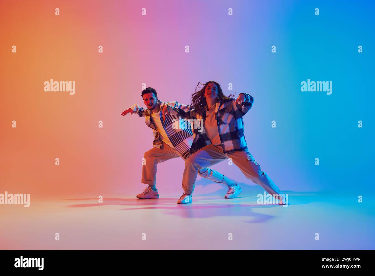 Man and woman, dancing synchronously in motion against gradient studio ...