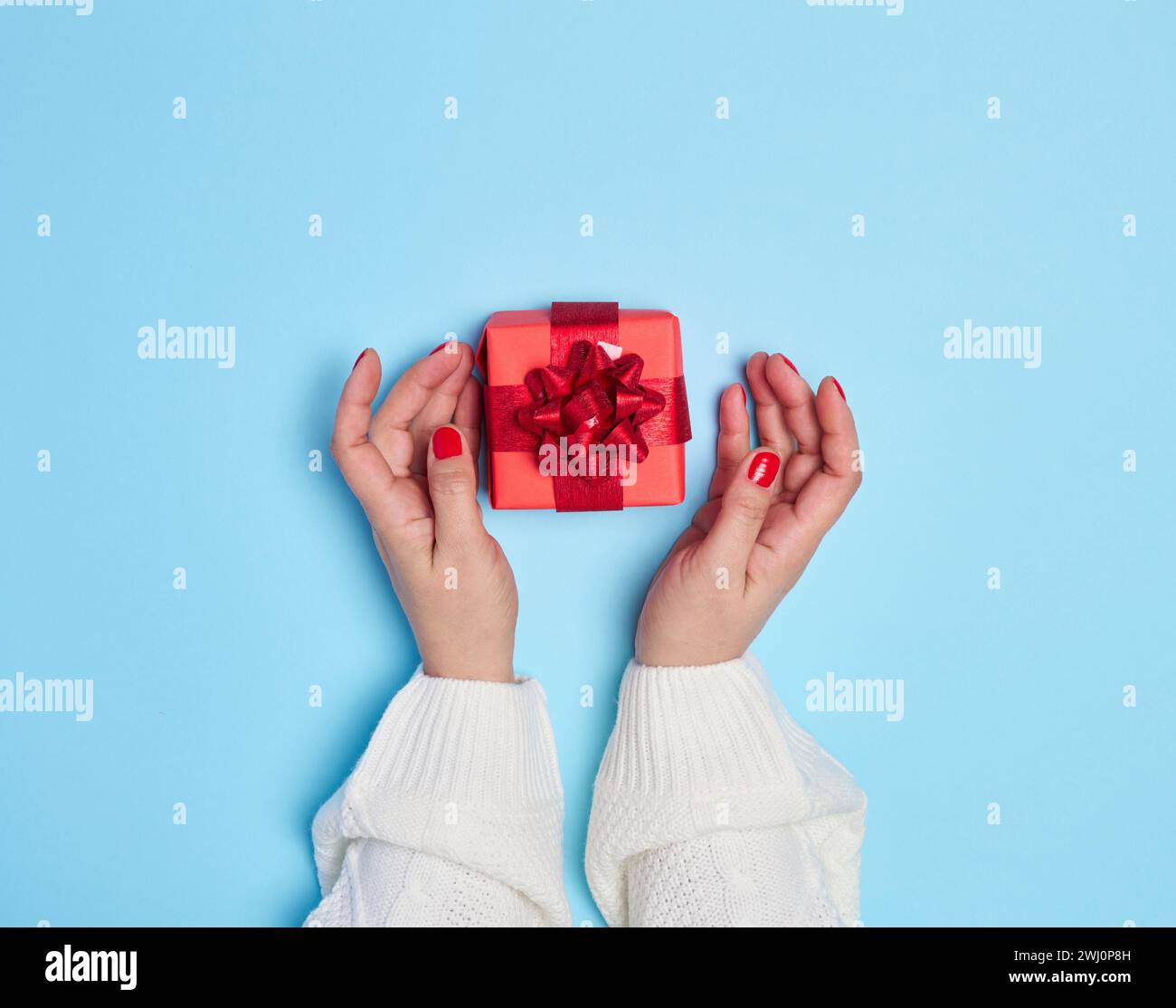 Female hands holding a gift box with a red ribbon on a blue background ...