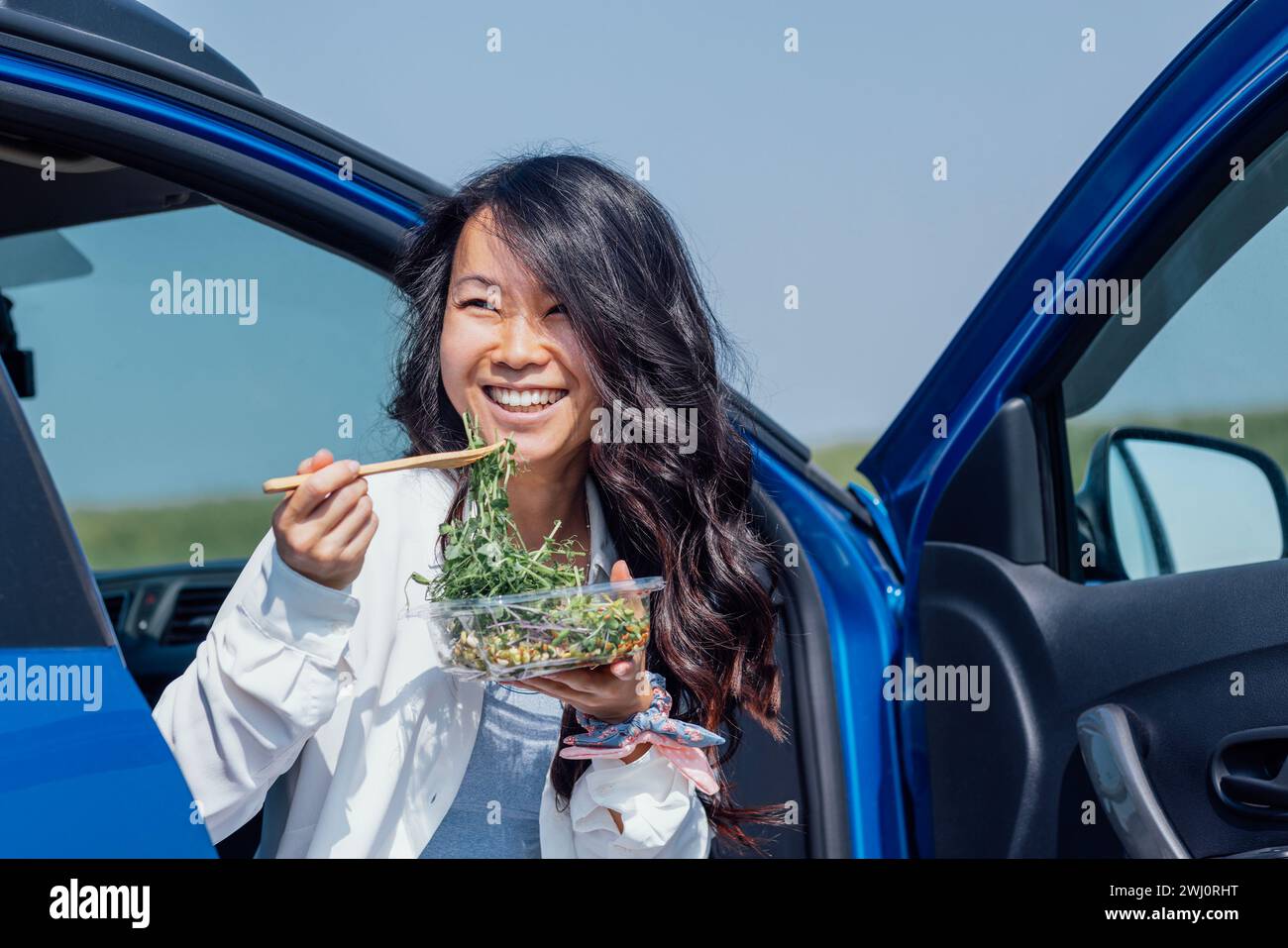 A young beautiful Korean woman in white clothes is eating a fresh salad ...
