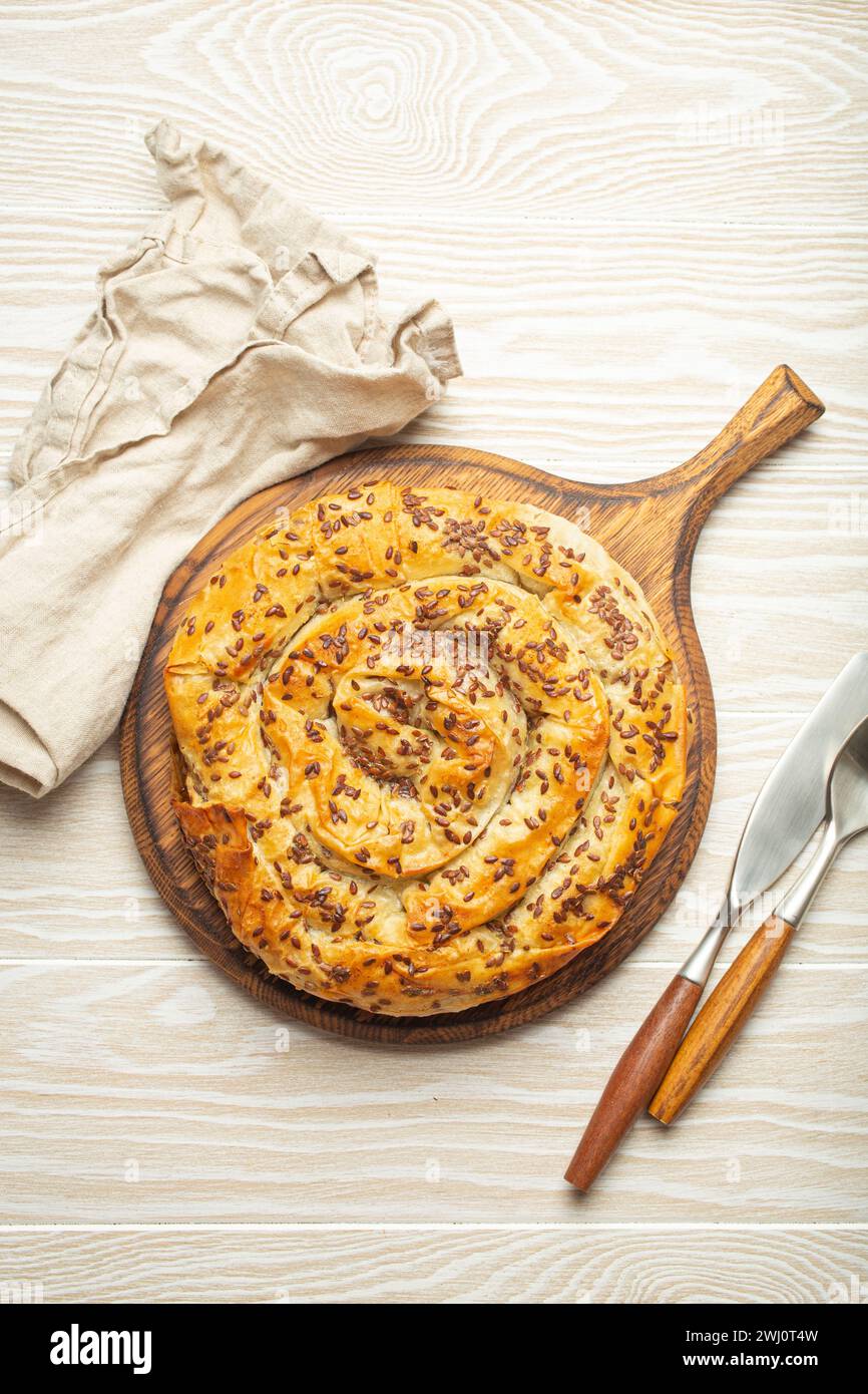 Burek made of filo dough with filling on cutting board, white wooden ...