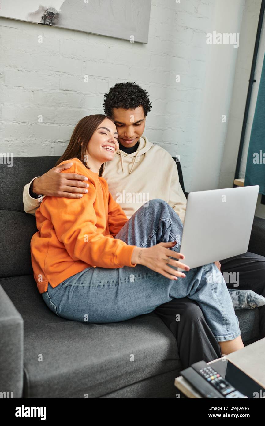 happy diverse couple snuggle on couch while watching movie on laptop ...