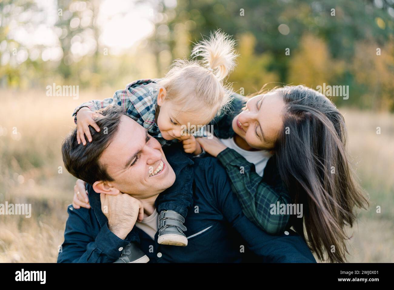 Mom and little girl look into the face of a laughing dad hugging him ...