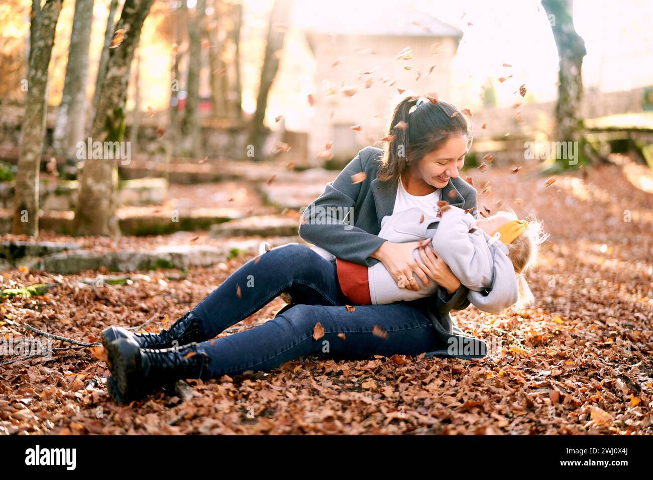 Smiling mom hugging little girl on her knees while sitting in autumn ...