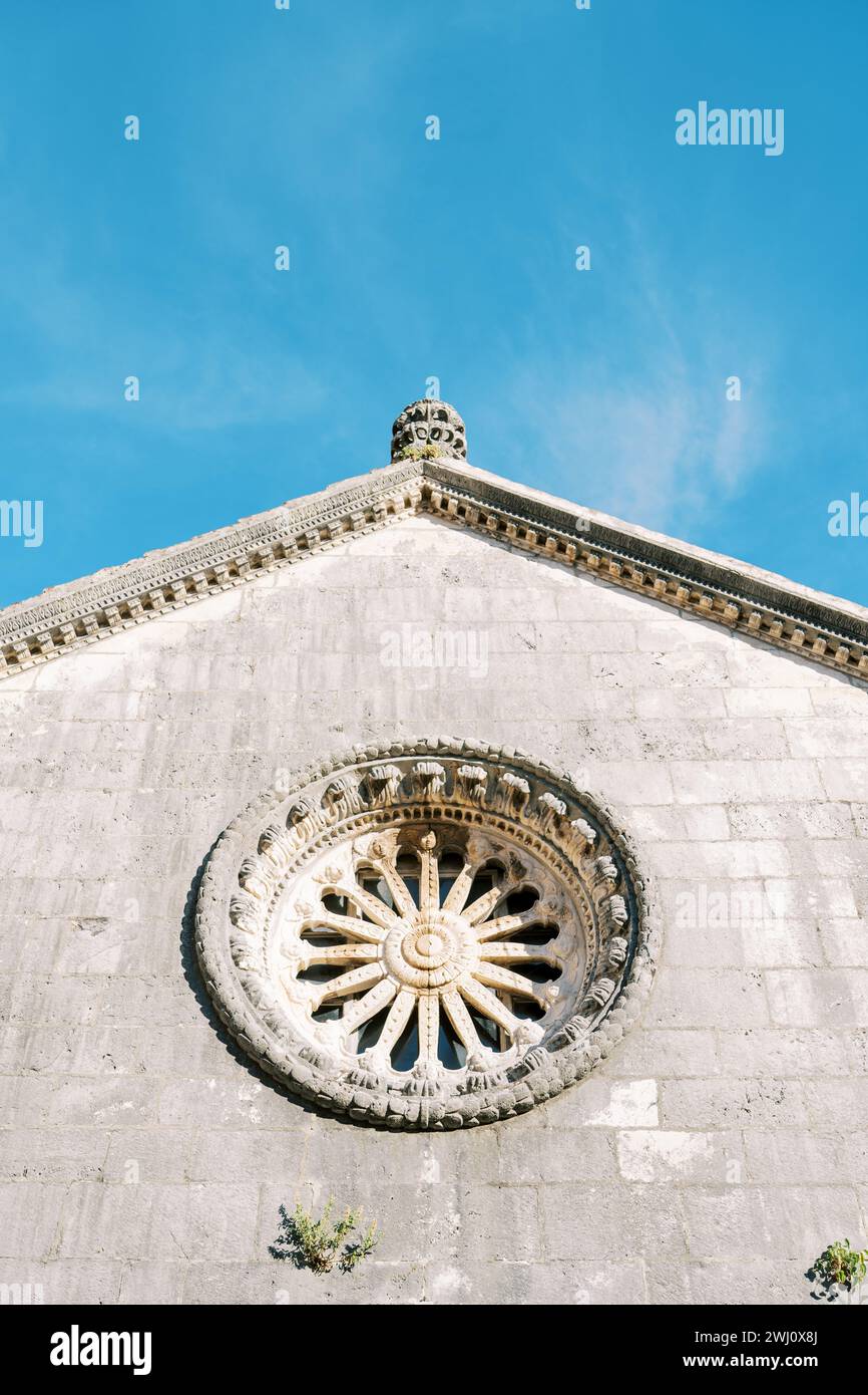 Rose window on the facade of an ancient stone church against a blue sky ...