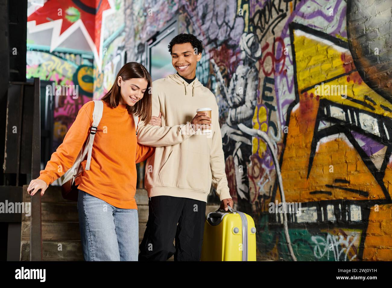 diverse couple smiling and walking next to each other on stairs with graffiti, man holding ...