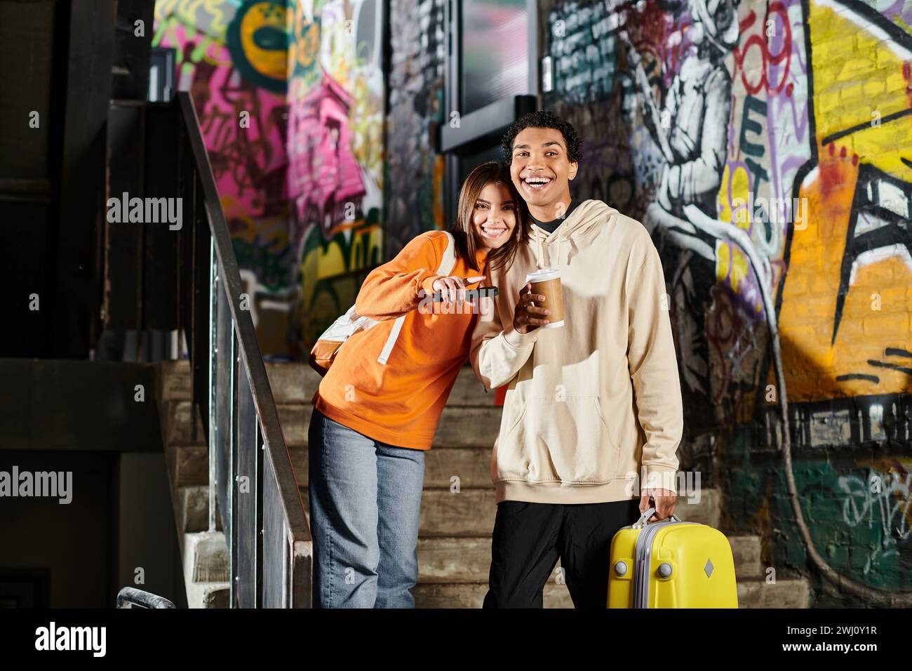 diverse couple smiling and standing next to each other on stairs with graffiti, man holding ...