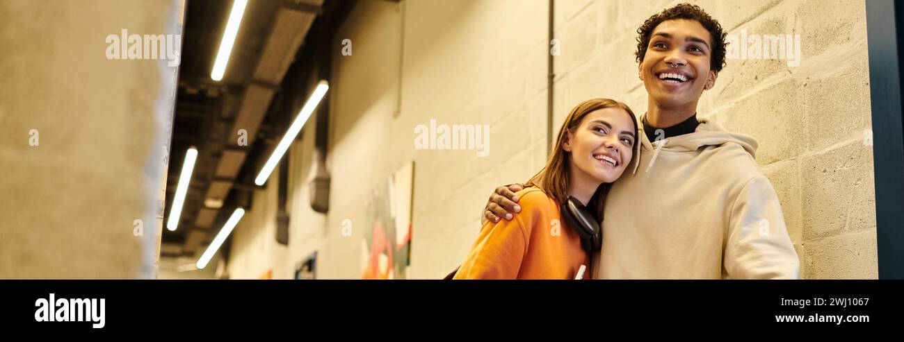 cheerful multicultural couple smiling and hugging in hall of hostel ...