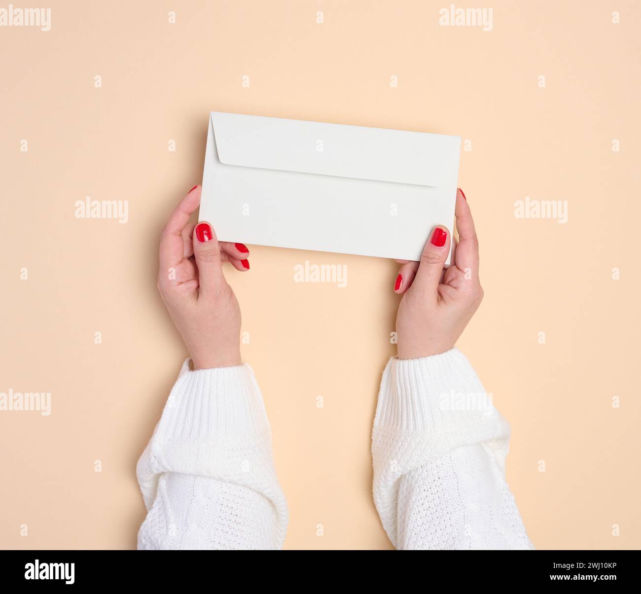 Two female hands holding a white rectangular envelope on a beige ...
