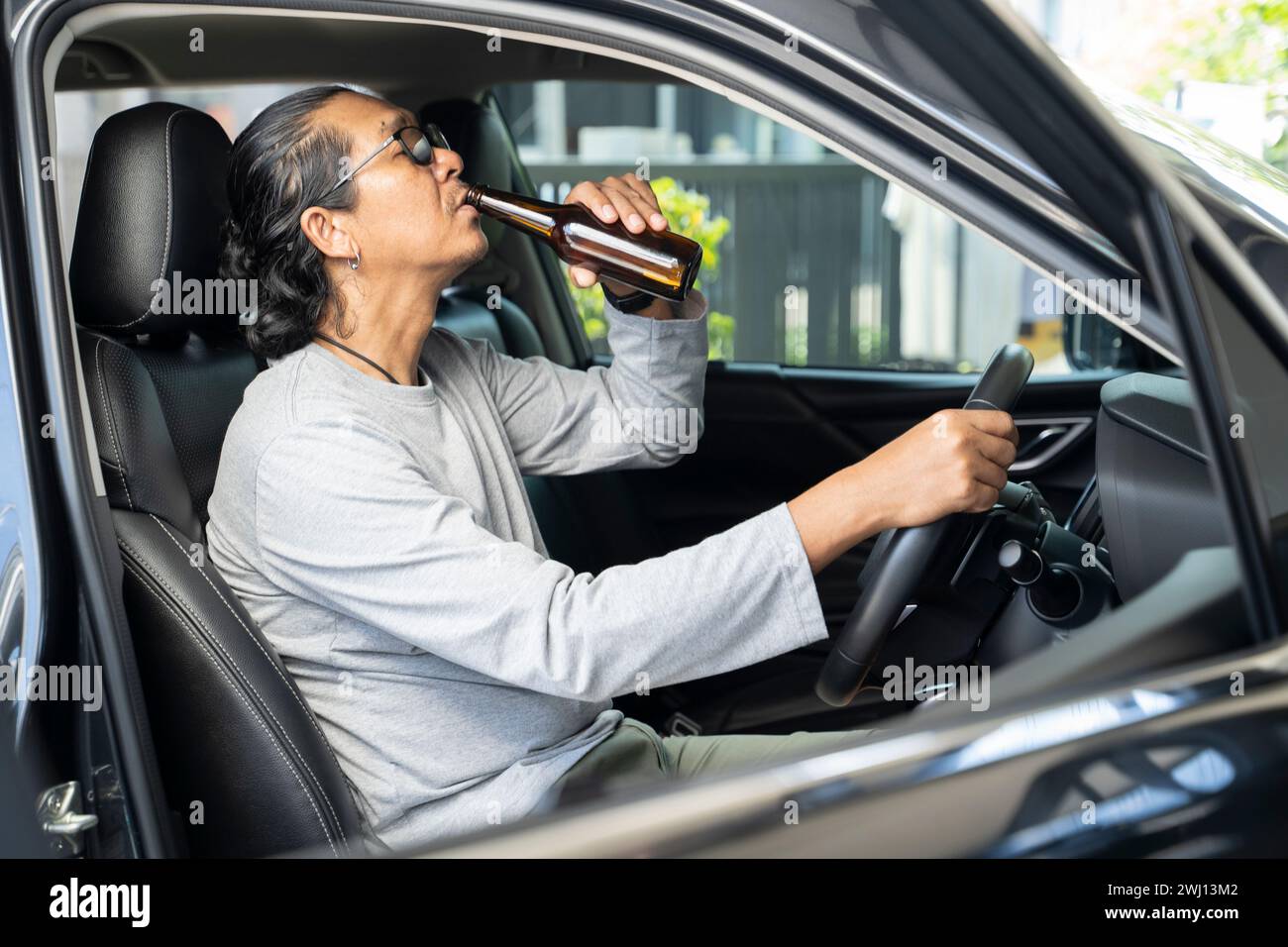 Drunk asian young man drives a car with a bottle of beer, Dangerous ...