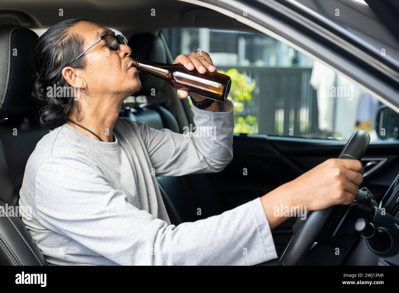 Drunk asian young man drives a car with a bottle of beer, Dangerous ...
