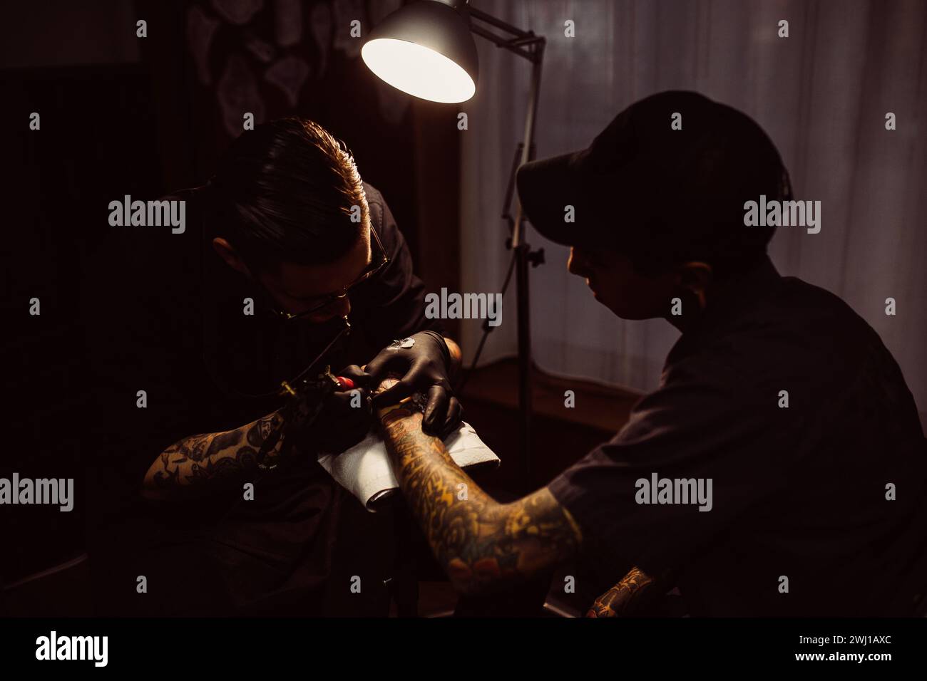 Tattoo artist inking a client in a dimly lit studio, showcasing the art ...
