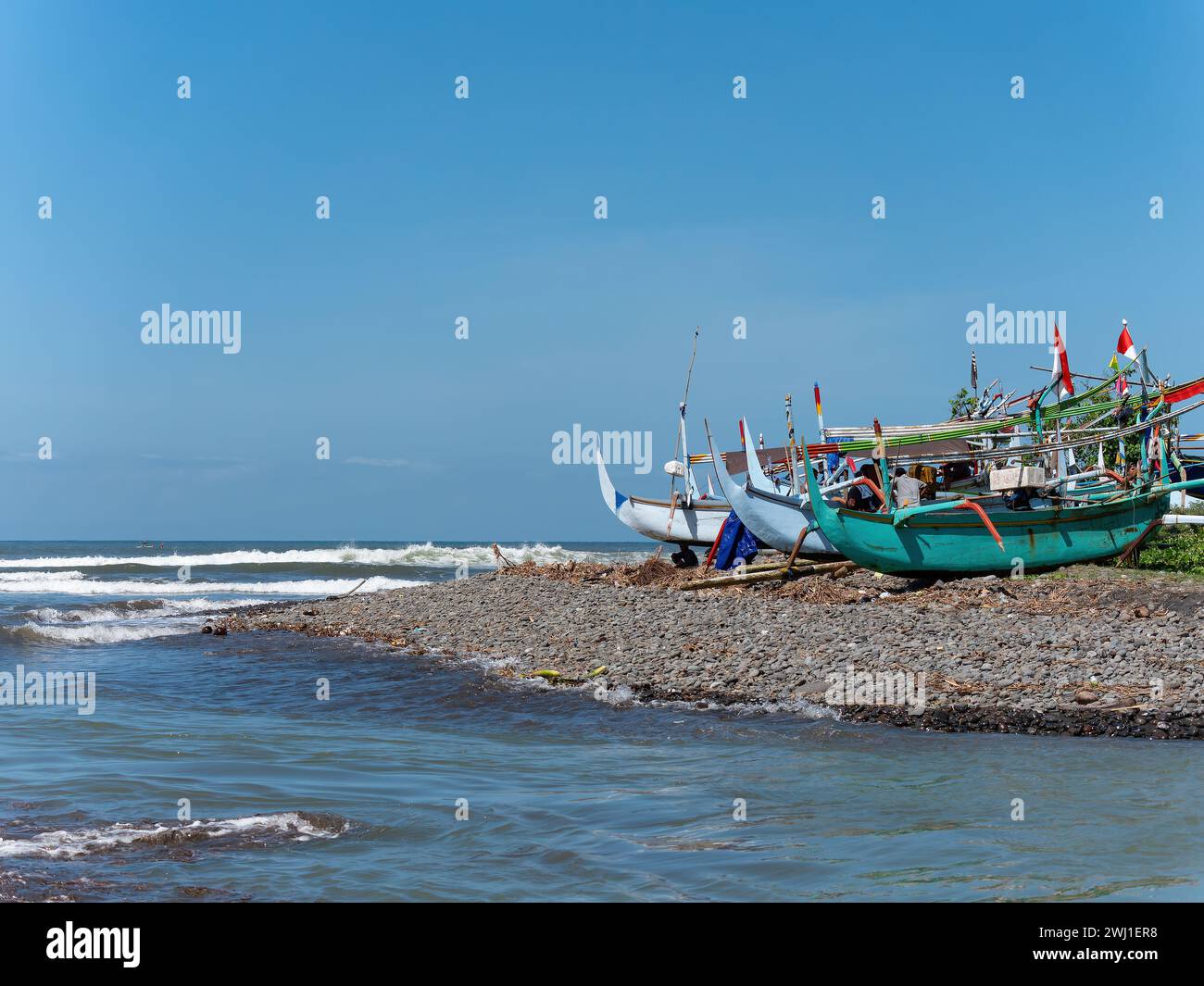 Traditional Indonesian fishing boat with outriggers on a stony beach in ...