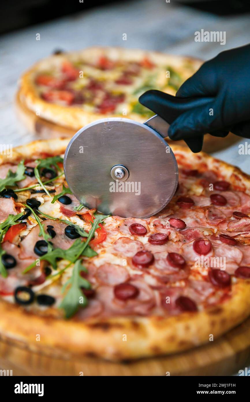 Cutting pizza on slices with special knife. Fresh pizza at background ...