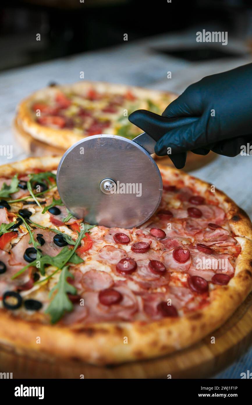 Cutting pizza on slices with special knife. Fresh pizza at background ...