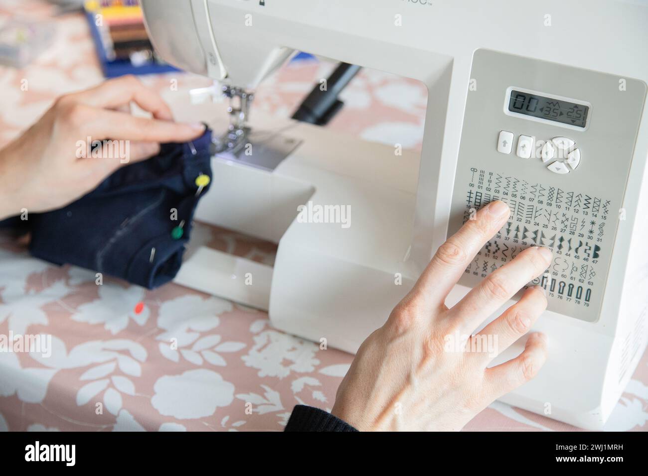 Detail of a hand pressing the button to select a stitch for machine ...