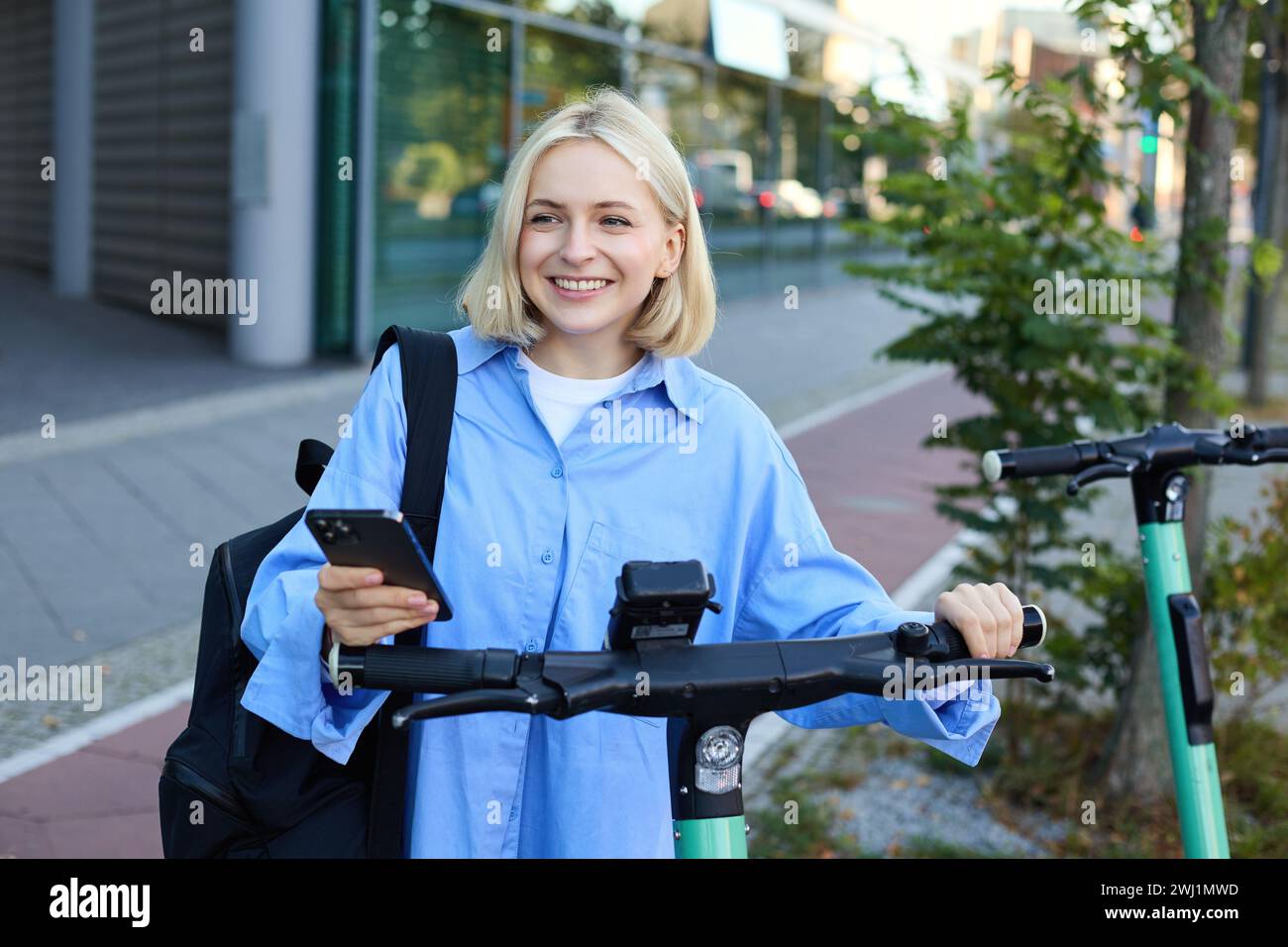 Portrait of young smiling woman, unlocks electric scooter, scans qr ...