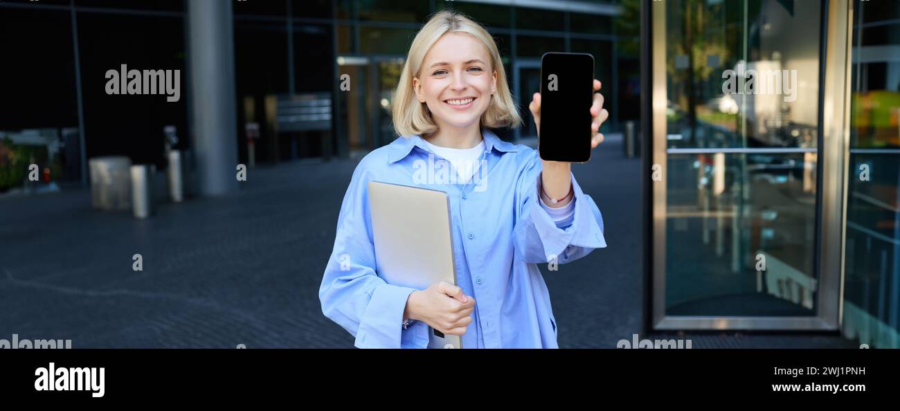 Portrait of beautiful young woman, student posing on street near campus ...
