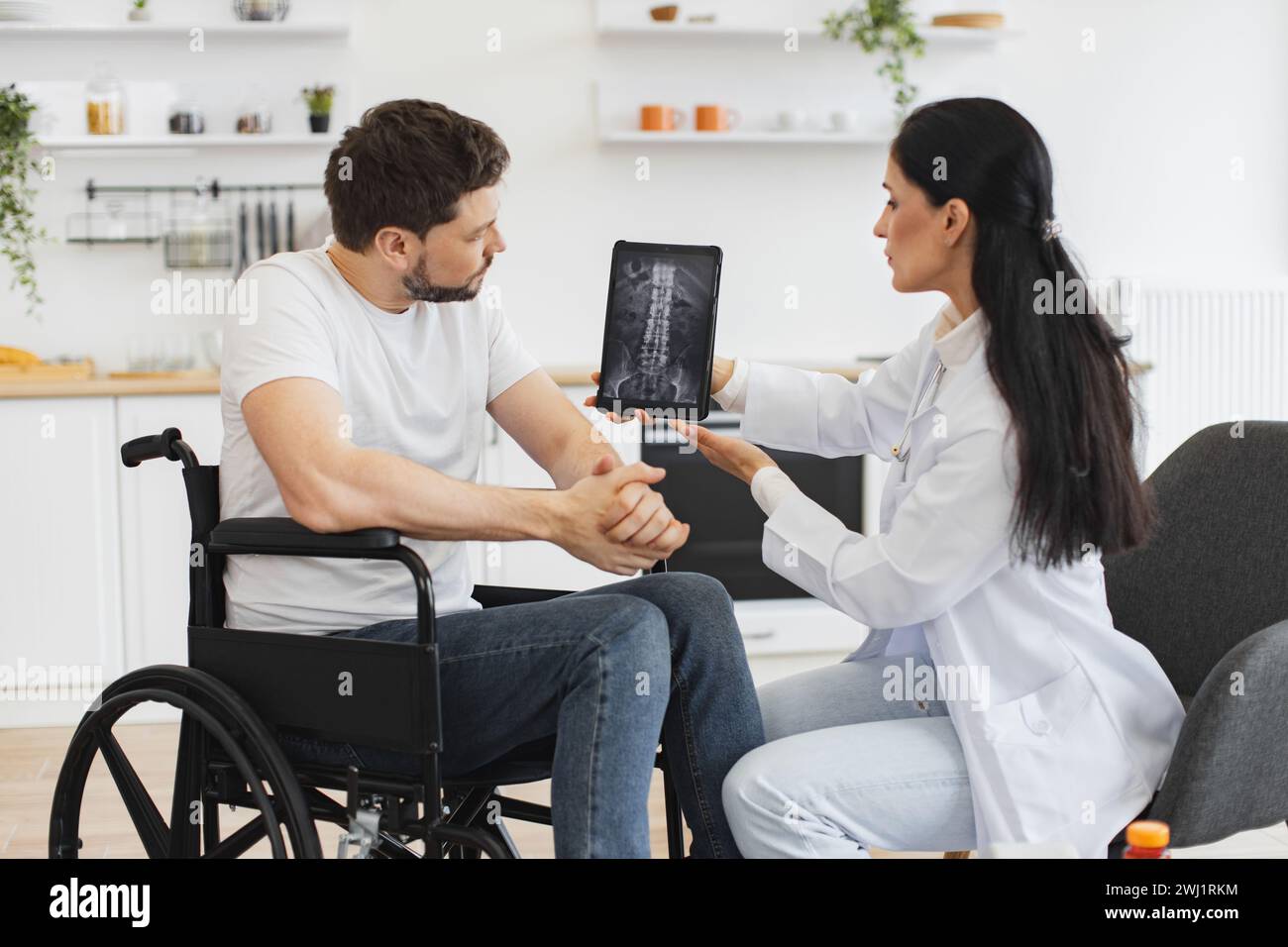 Nurse talking to man wheelchair user, showing x-ray scan of spine on ...