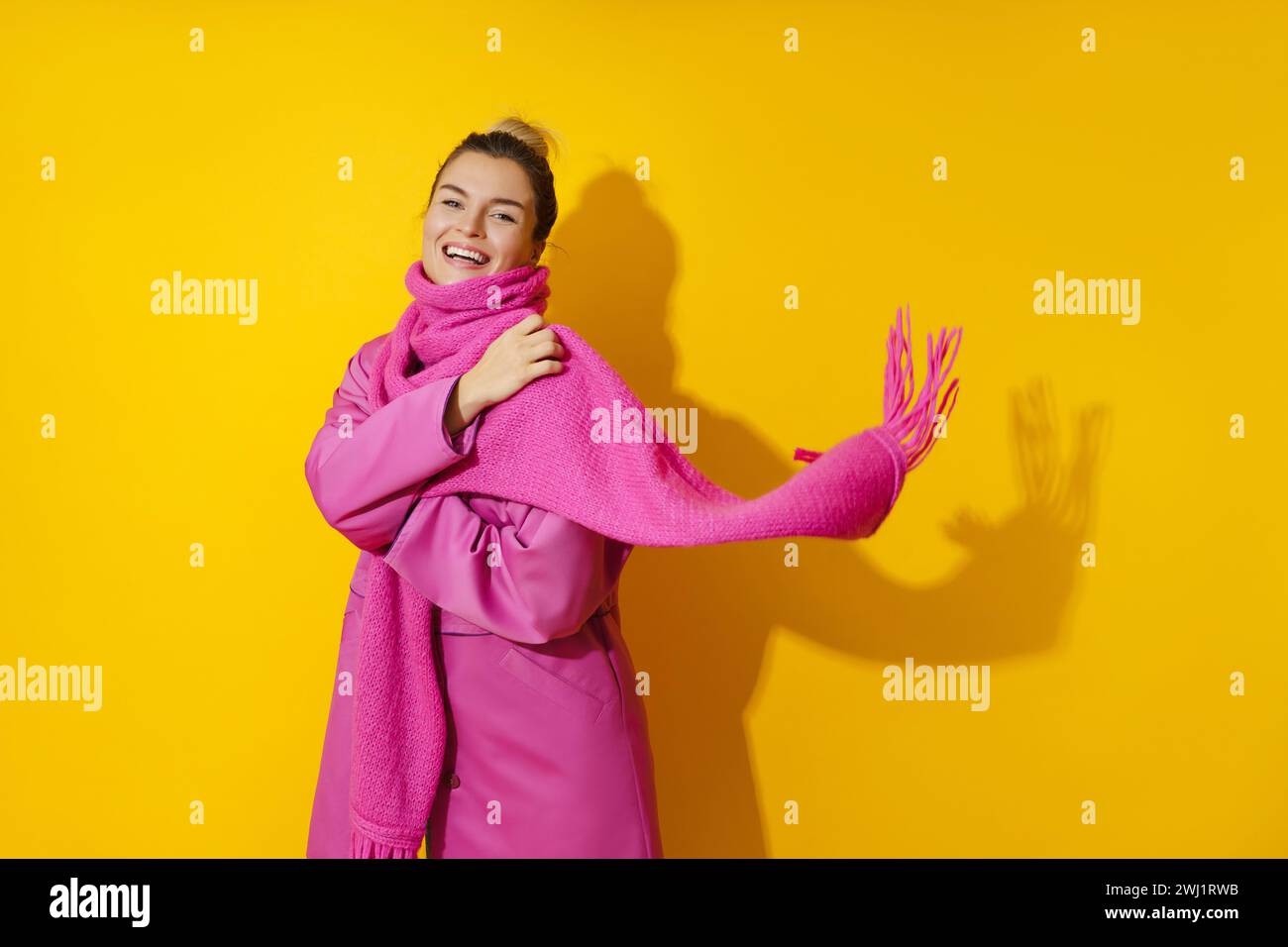 Young cheerful woman wearing pink coat and wool scarf against yellow ...