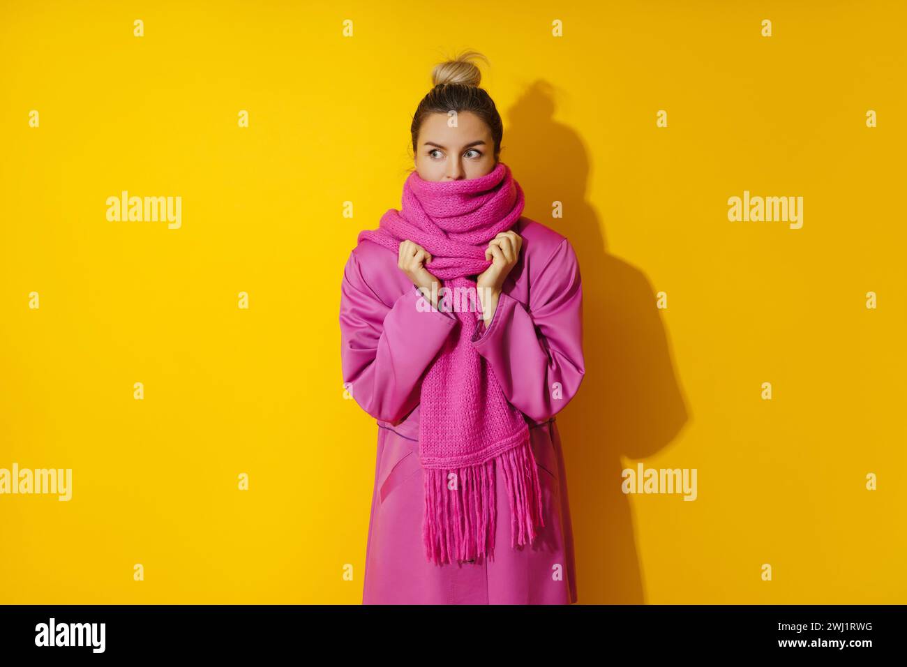 Young cheerful woman wearing pink coat and wool scarf against yellow ...