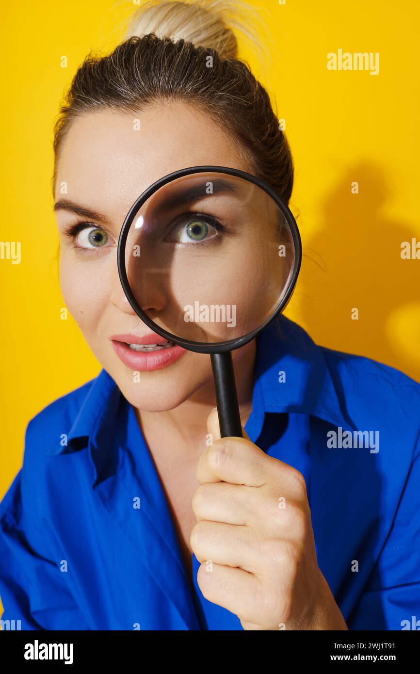 Curious woman is peering through magnifying glass with great interest ...