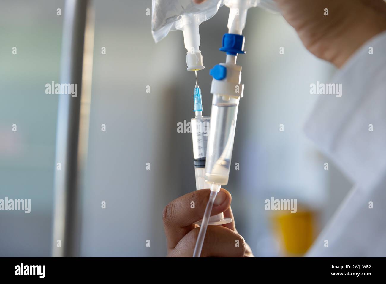 Hands of biracial male doctor preparing drip in sunny hospital room ...