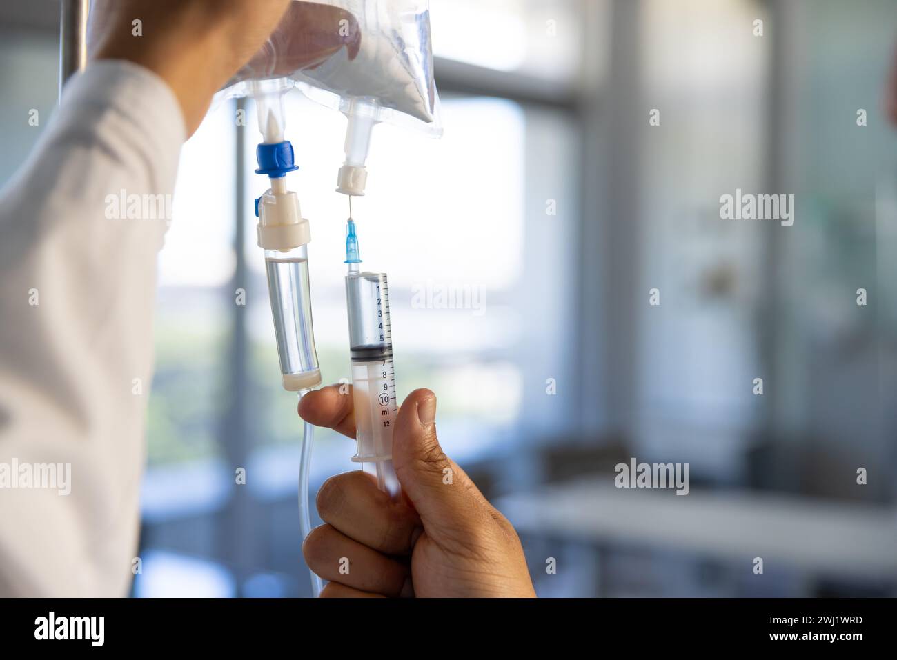 Hands of biracial male doctor preparing drip in sunny hospital room ...