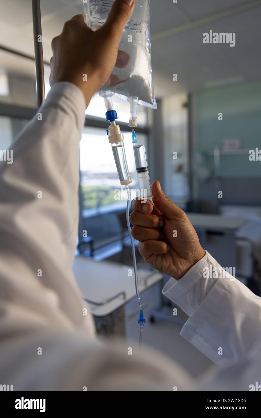 Hands of biracial male doctor preparing drip in sunny hospital room ...