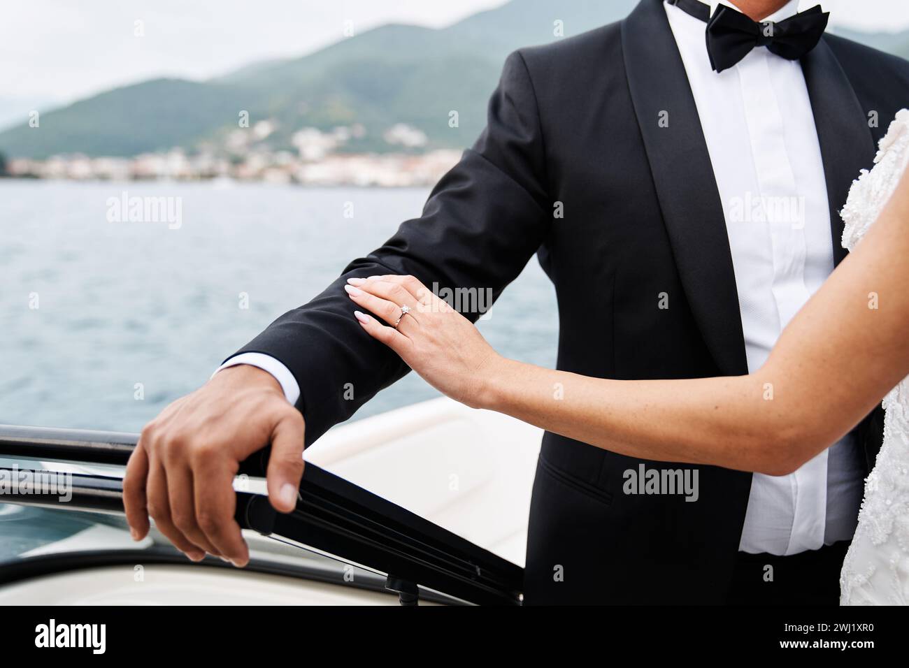 Bride touches groom hand while standing in a boat floating on the sea ...