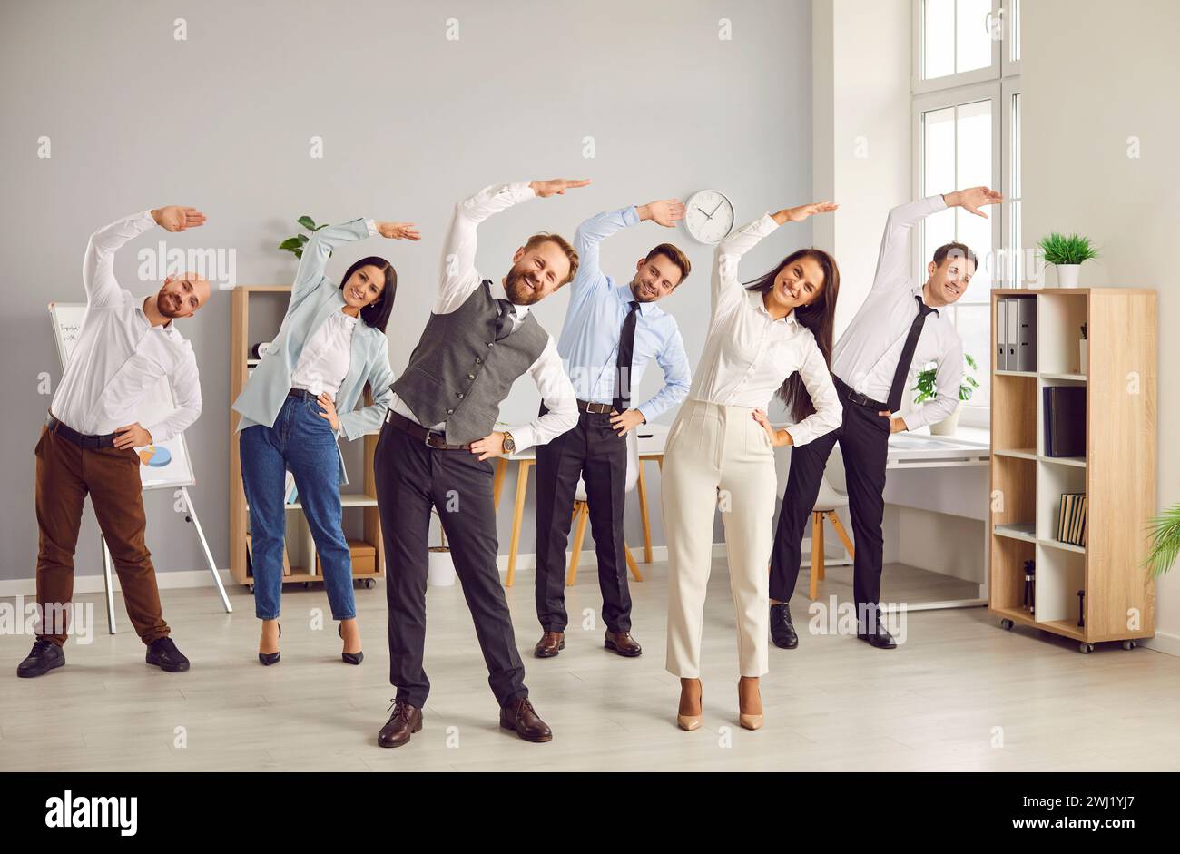 Happy smiling young business people doing stretching exercises in ...