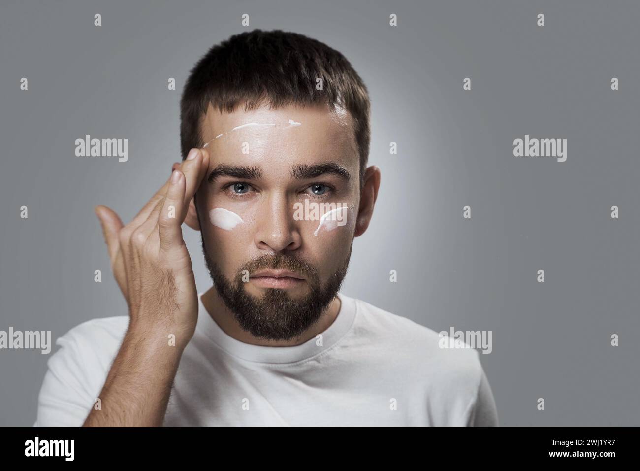 Young man is applying moisturizing cream on his face Stock Photo - Alamy