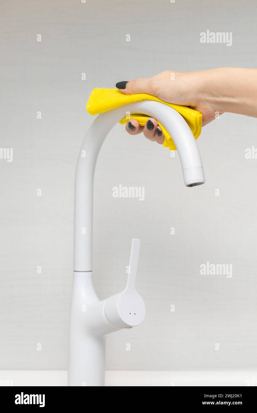woman wiping faucet with rag in kitchen. hand wipes a white kitchen ...