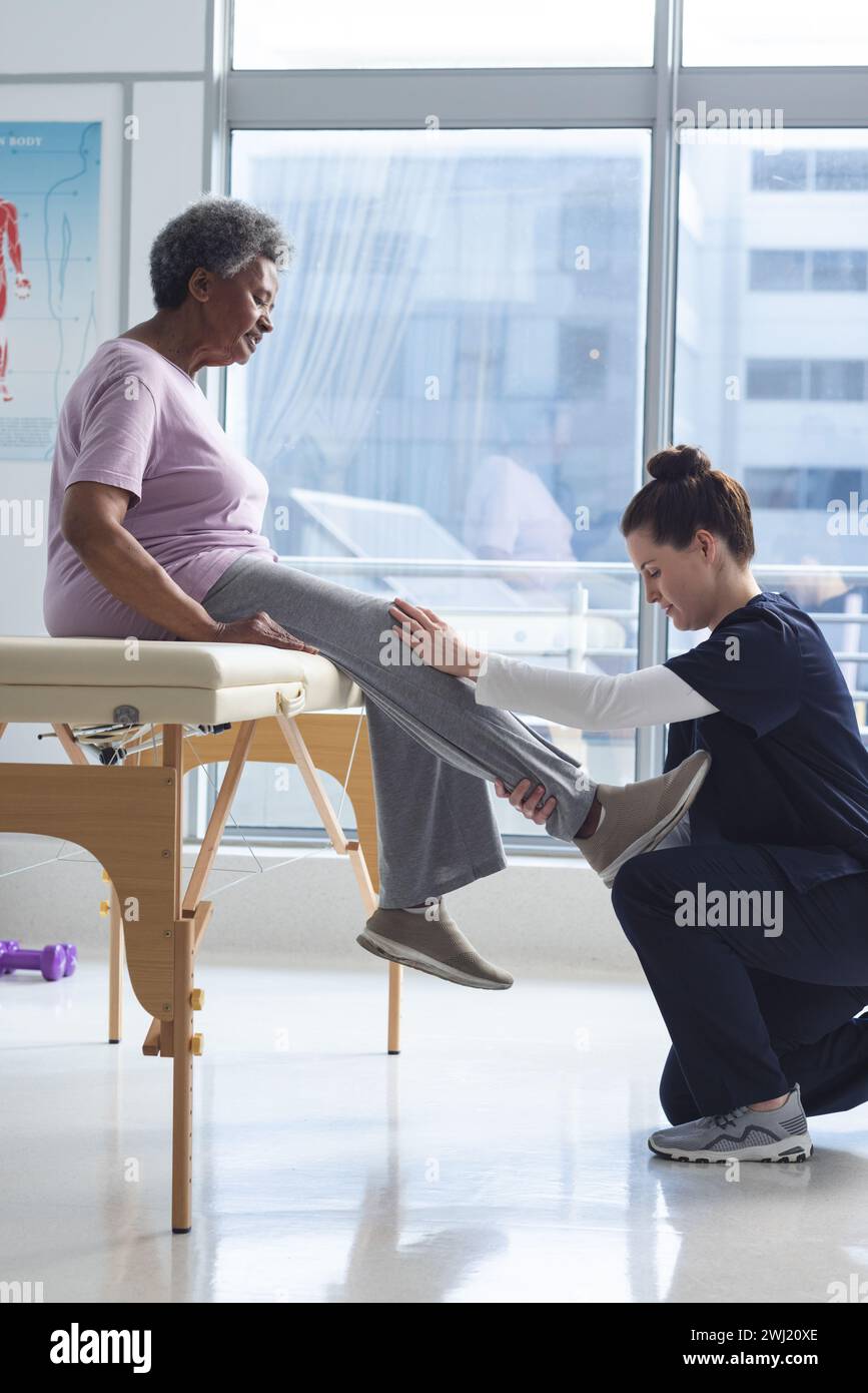 Diverse senior female patient exercising leg and female doctor advising ...