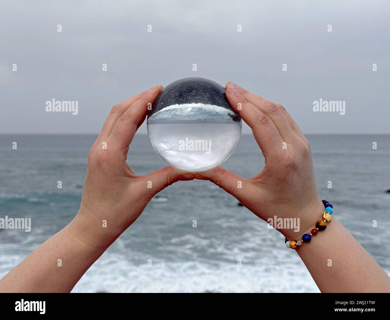 Hands holding crystal ball on ocean shore Stock Photo - Alamy