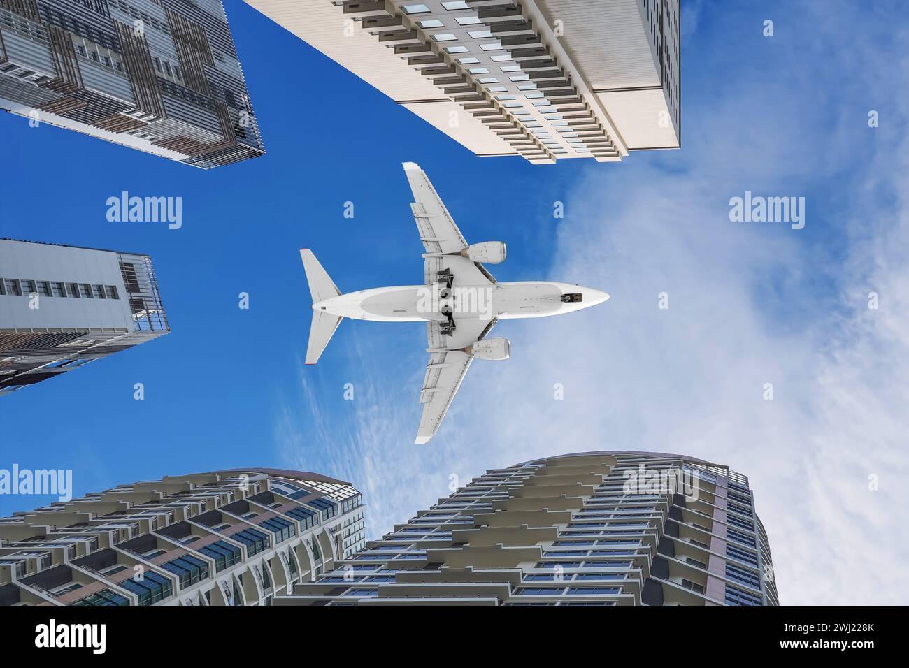 Airplane jet flying above in the sky among tall buildings in a modern ...