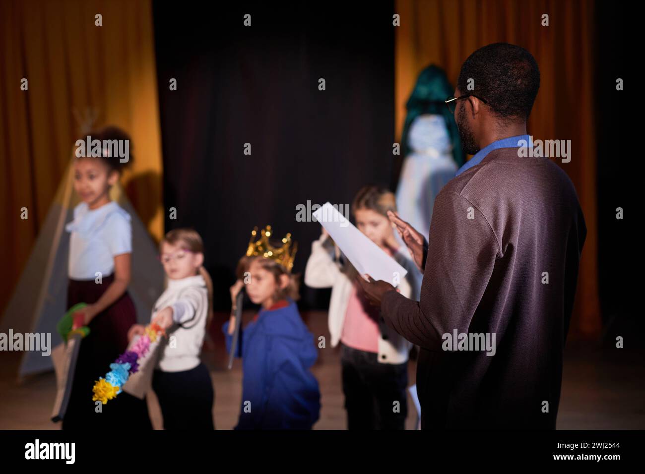 Back view of Black drama teacher directing school play with group of ...
