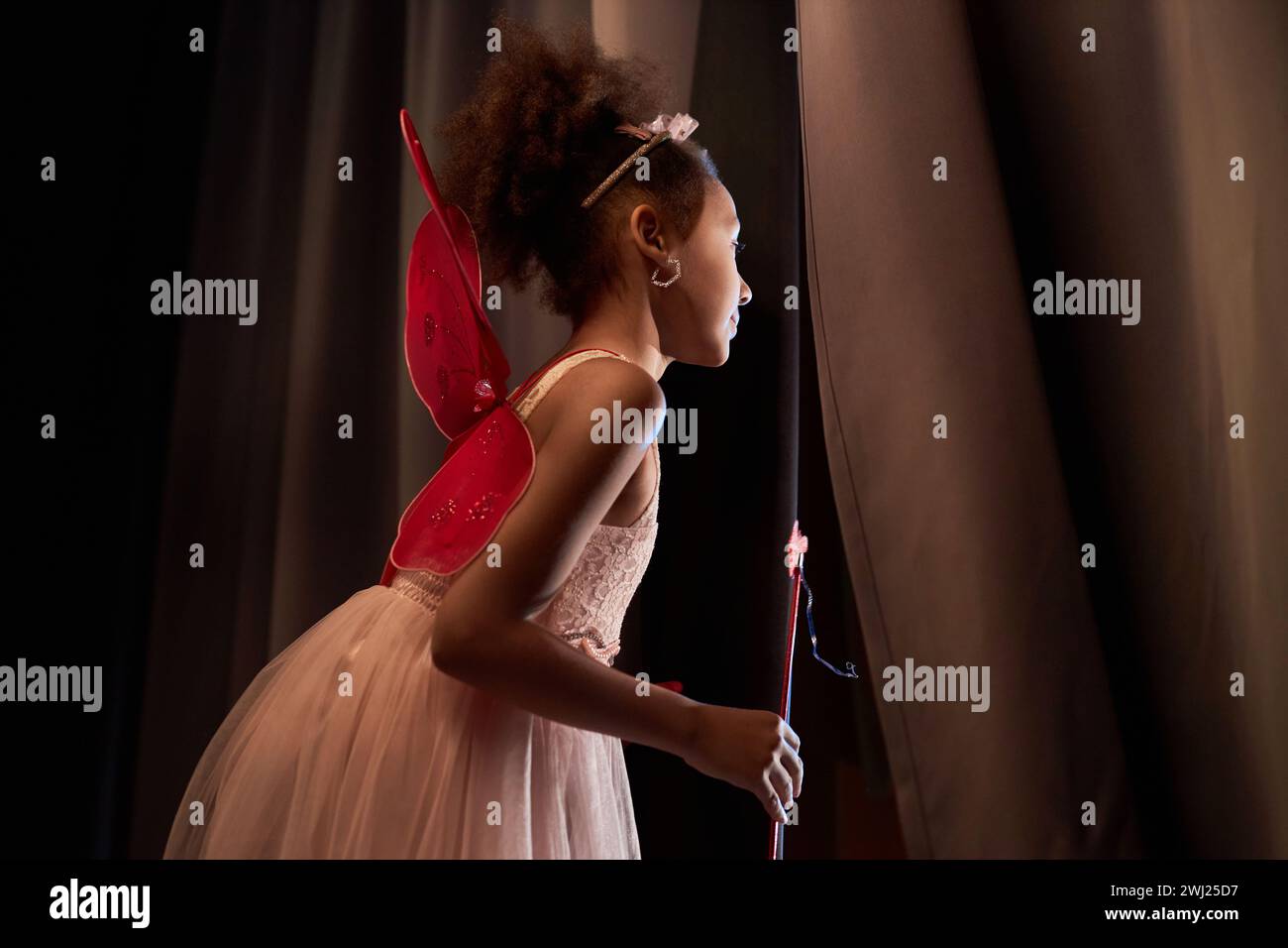 Side view young Black girl wearing fairy costume with wings peeking ...