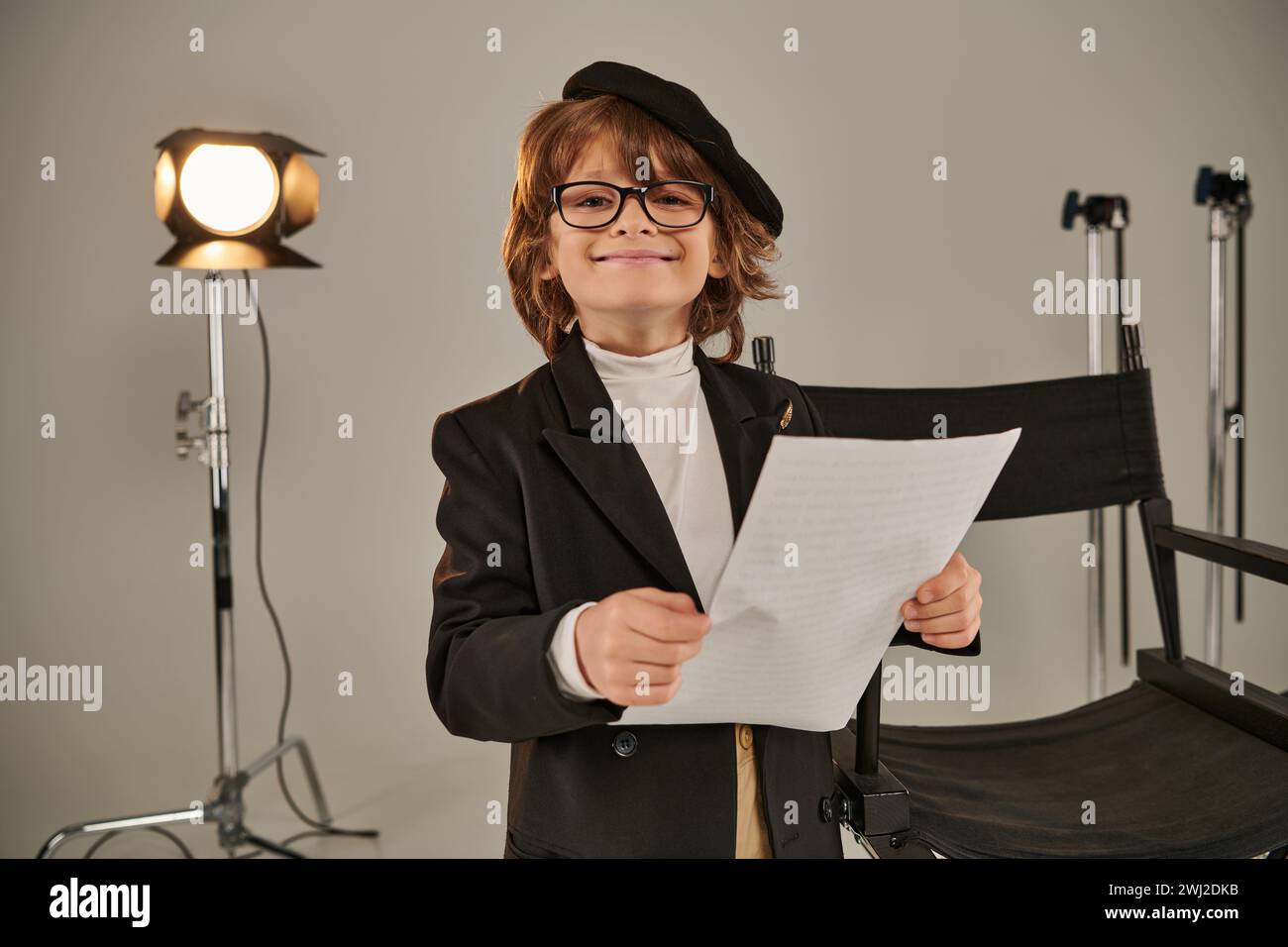cheerful kid in glasses and beret reading screenplay on papers, boy as ...